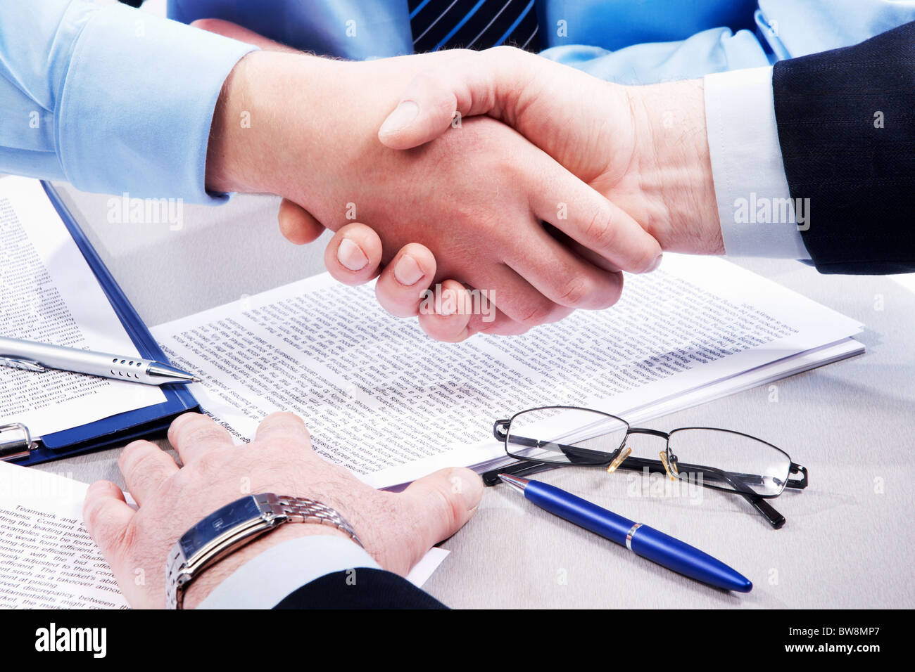 Close-up of business handshake over workplace with documents, pens ...