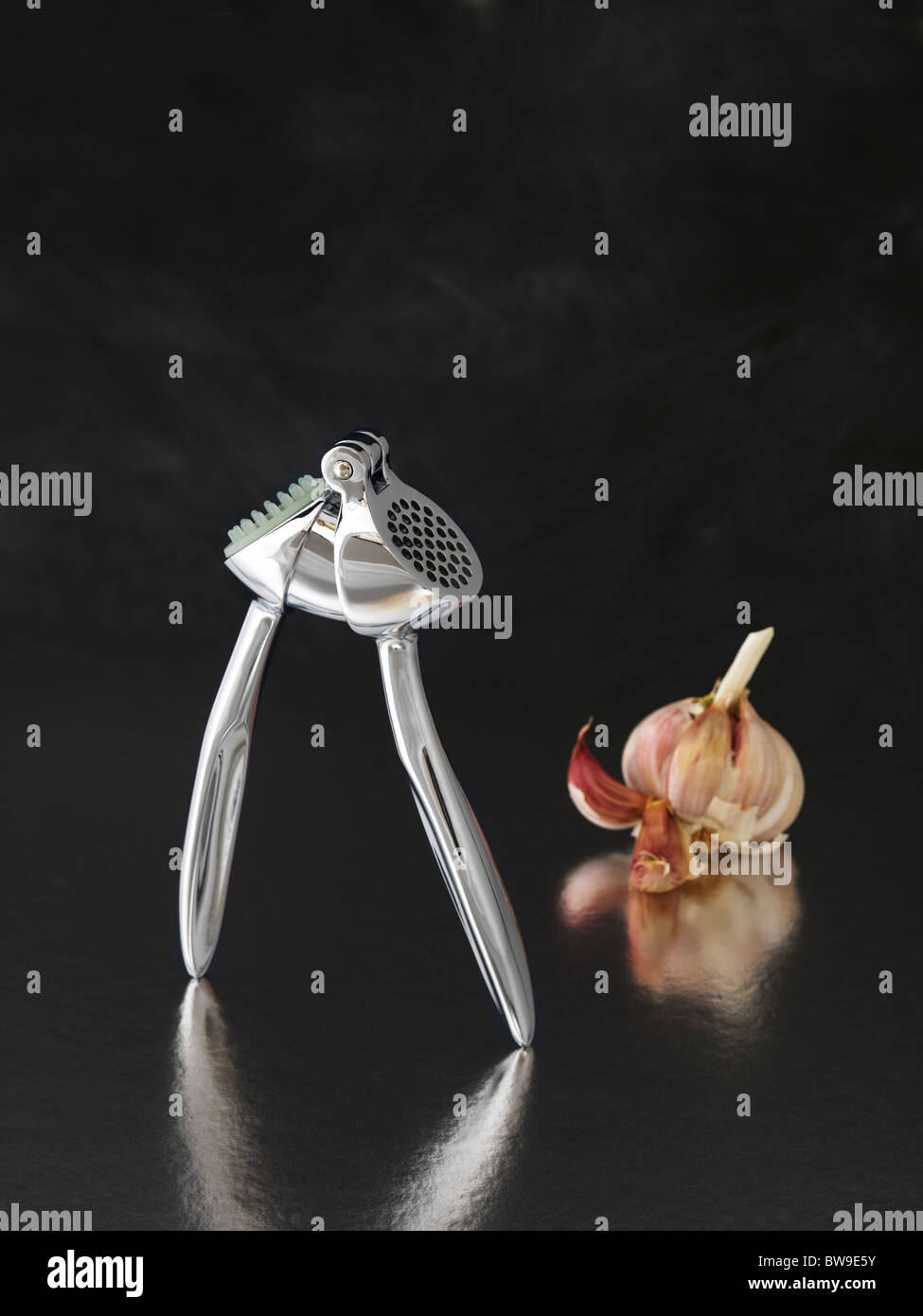 A garlic crusher or press and bulb of garlic on a grey background Stock ...