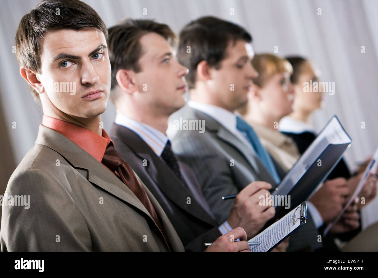Image of confident young man looking at camera with row of people on ...