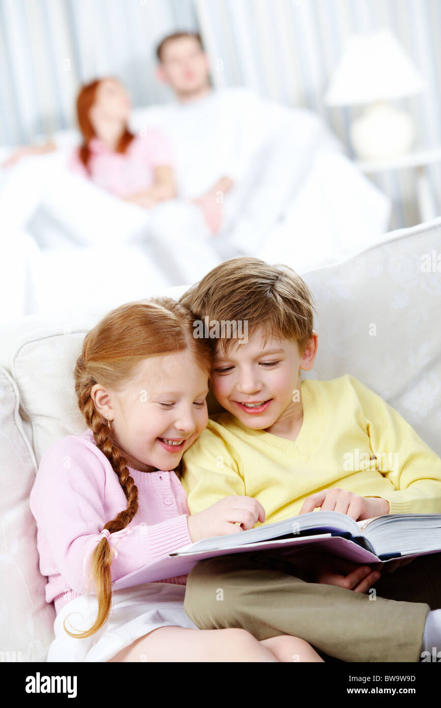 Portrait of happy children reading book while sitting on sofa at home ...
