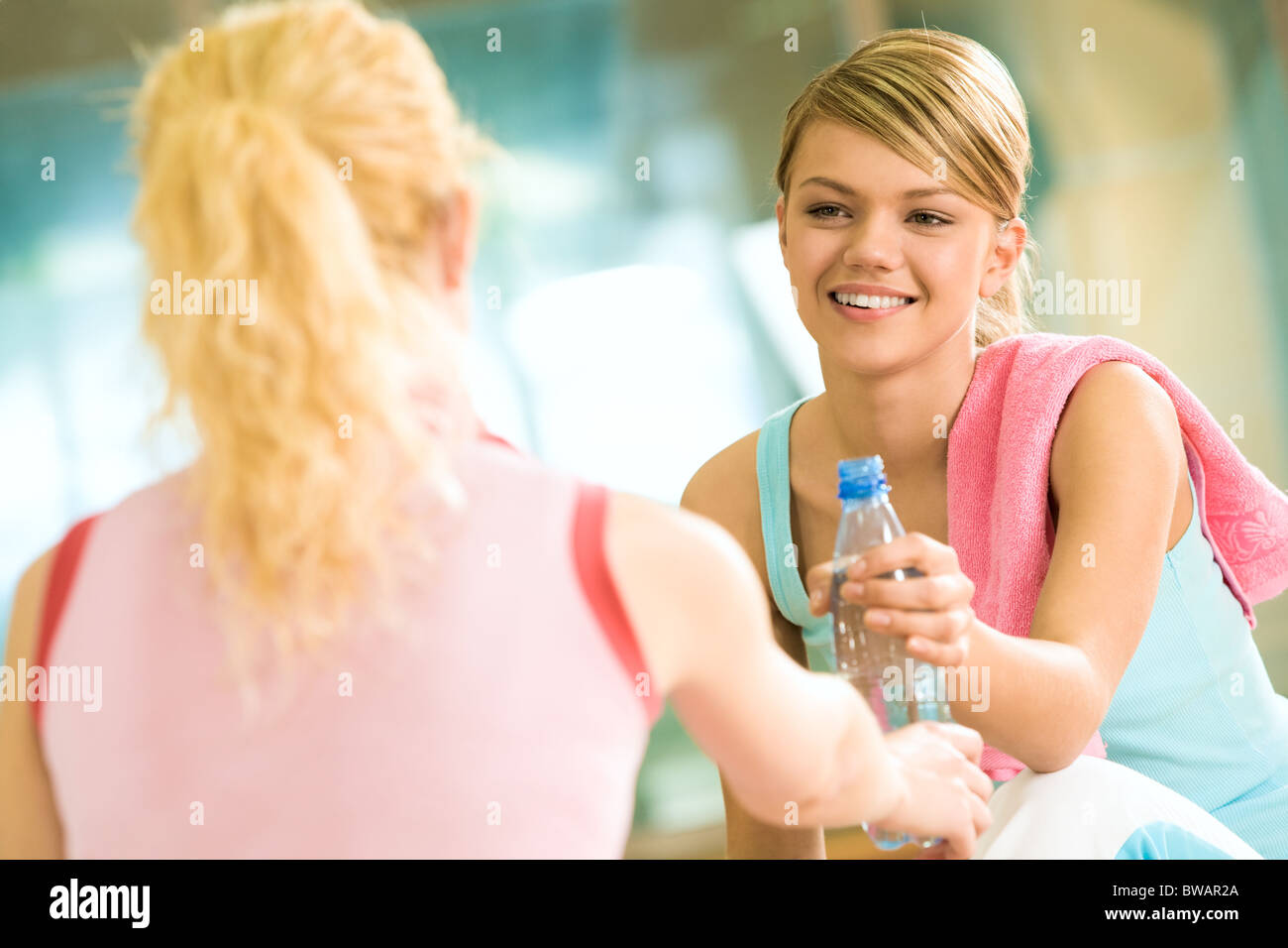 Generous girl giving bottle of water to the friend in front of her ...