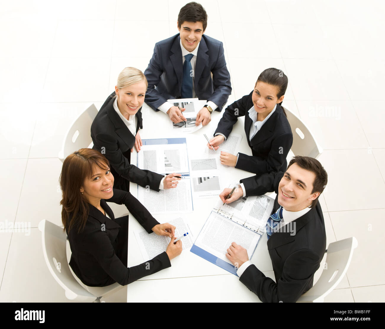 Several white collar workers sitting around table and looking upwards ...