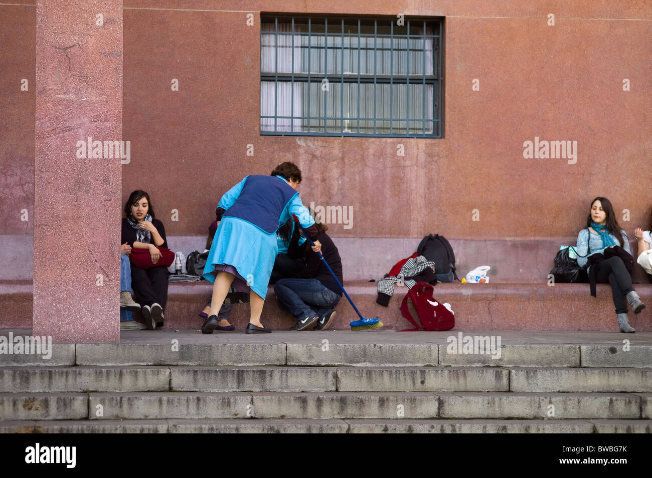 Woman sweeping around university students relaxing, Santiago, Chile ...