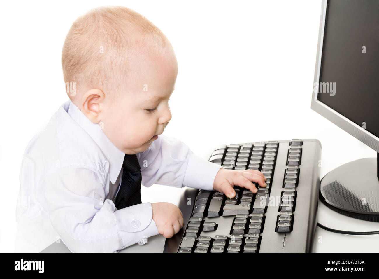 Photo of cute baby typing on keyboard with monitor in front of him ...