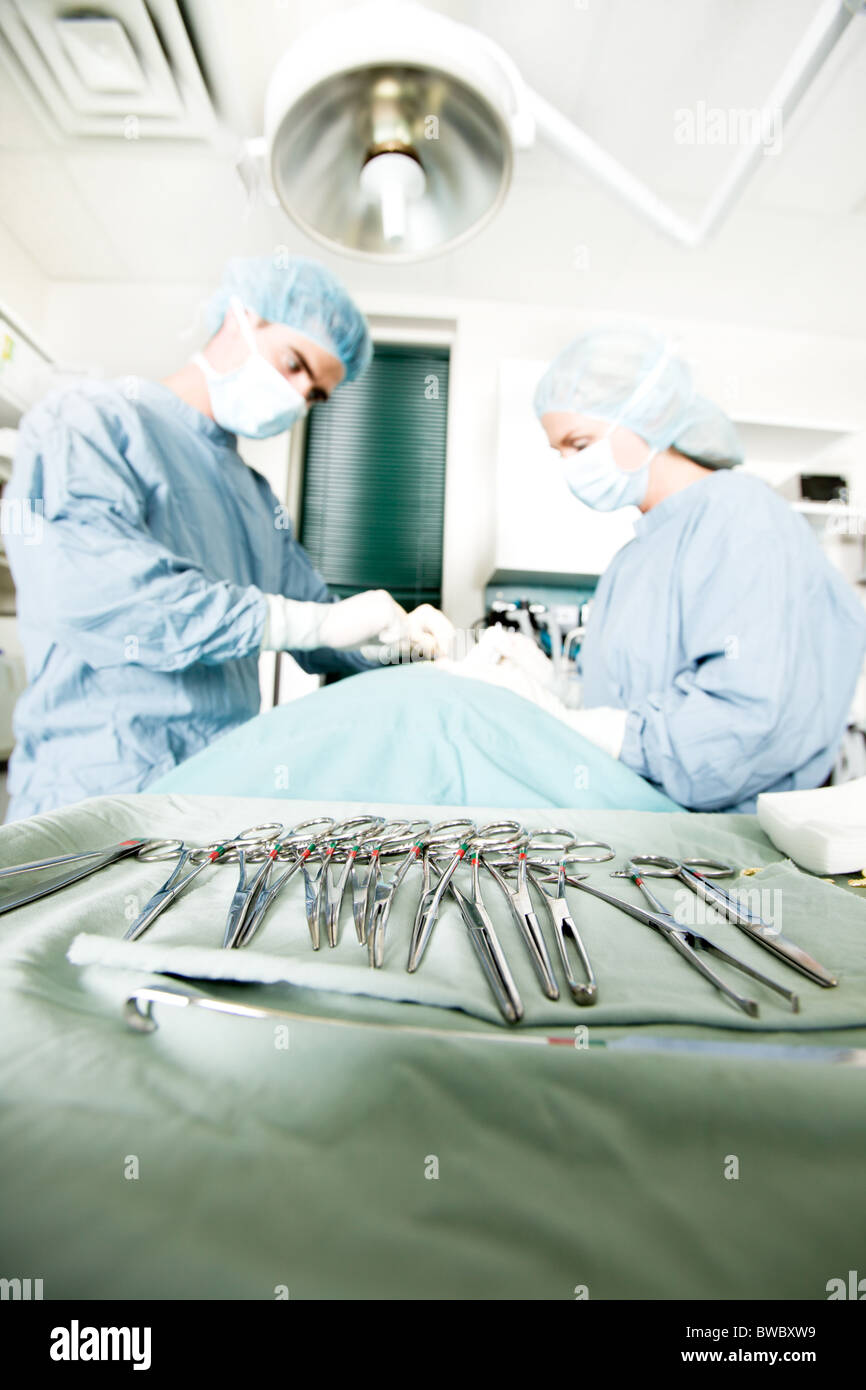 A row of sterile surgery instruments with live surgery being performed ...