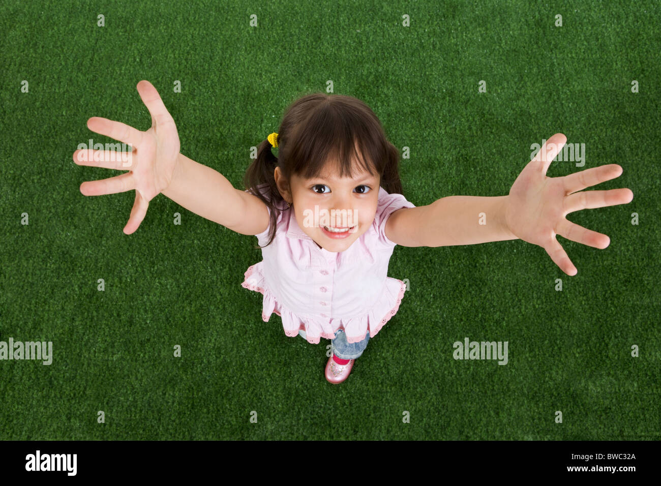 Above view of happy child standing on green grass and raising her arms ...