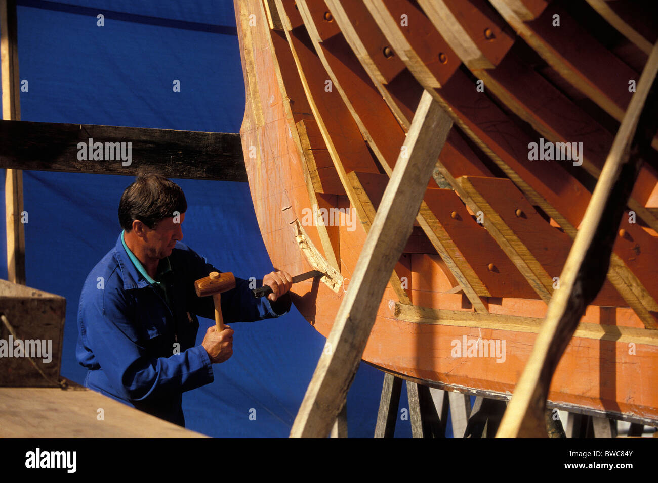Shipwright hammering a chisel into the hull of replica tuna boat ...
