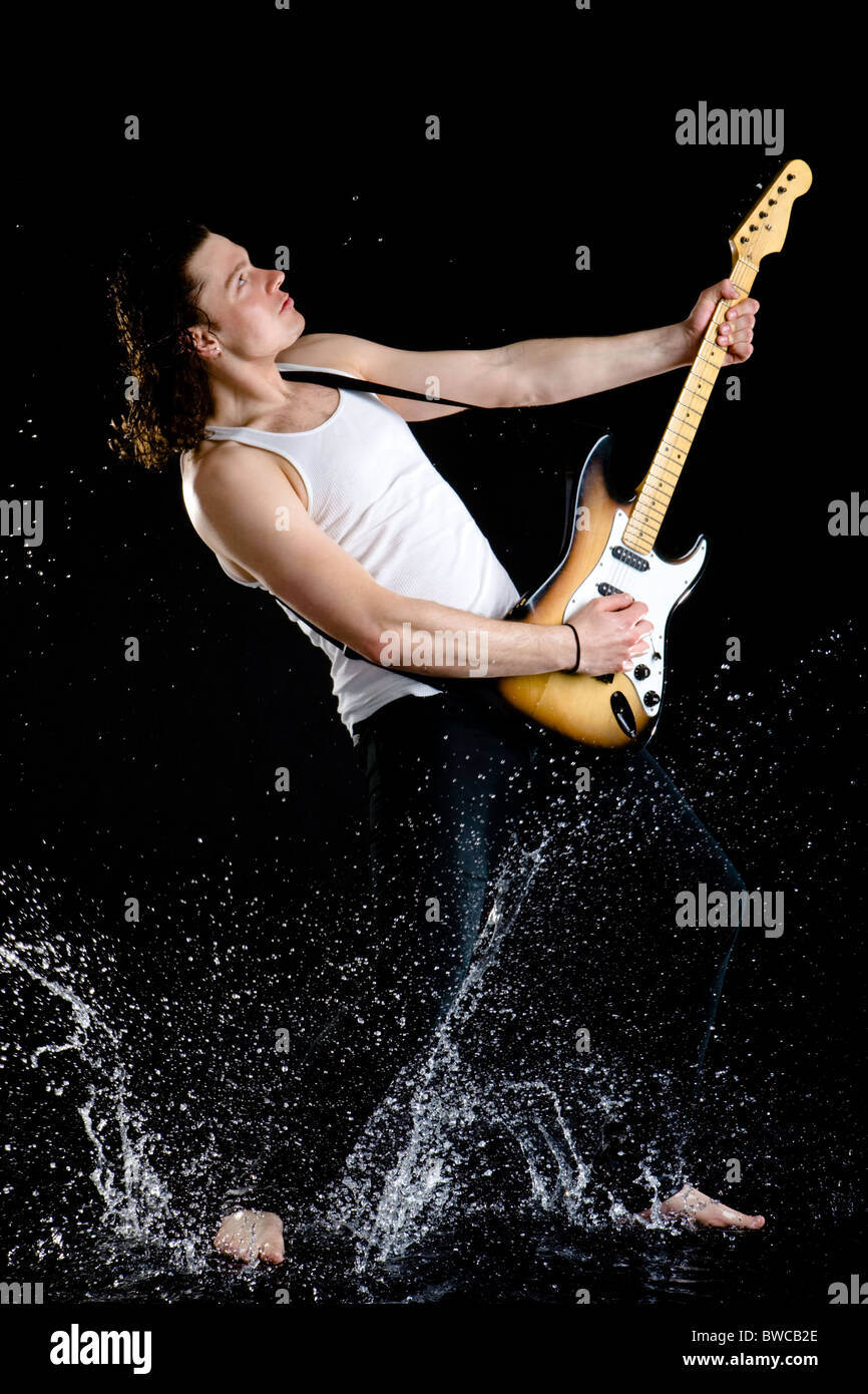 Portrait of young performer playing electrical guitar in water splashes ...