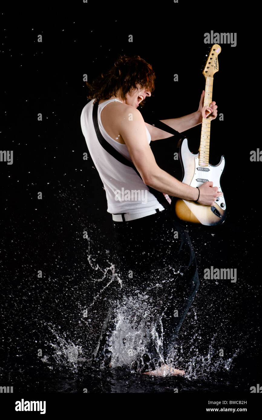 Portrait of young performer playing electrical guitar in water splashes ...