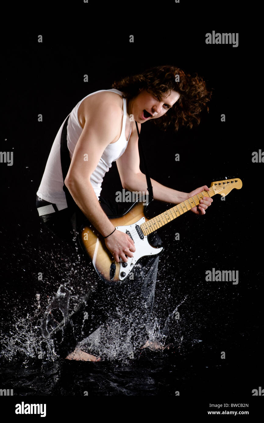 Portrait of young guitarist playing instrument while walking in water ...
