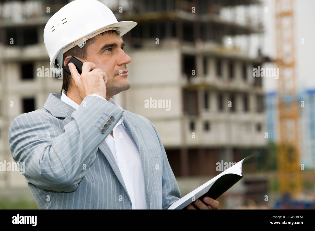 Portrait of confident foreman calling by the phone and holding document ...