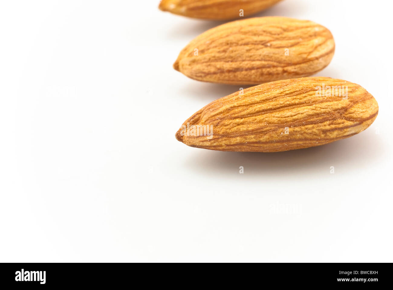 Three shelled almonds, in a row in right half of frame, on white ...