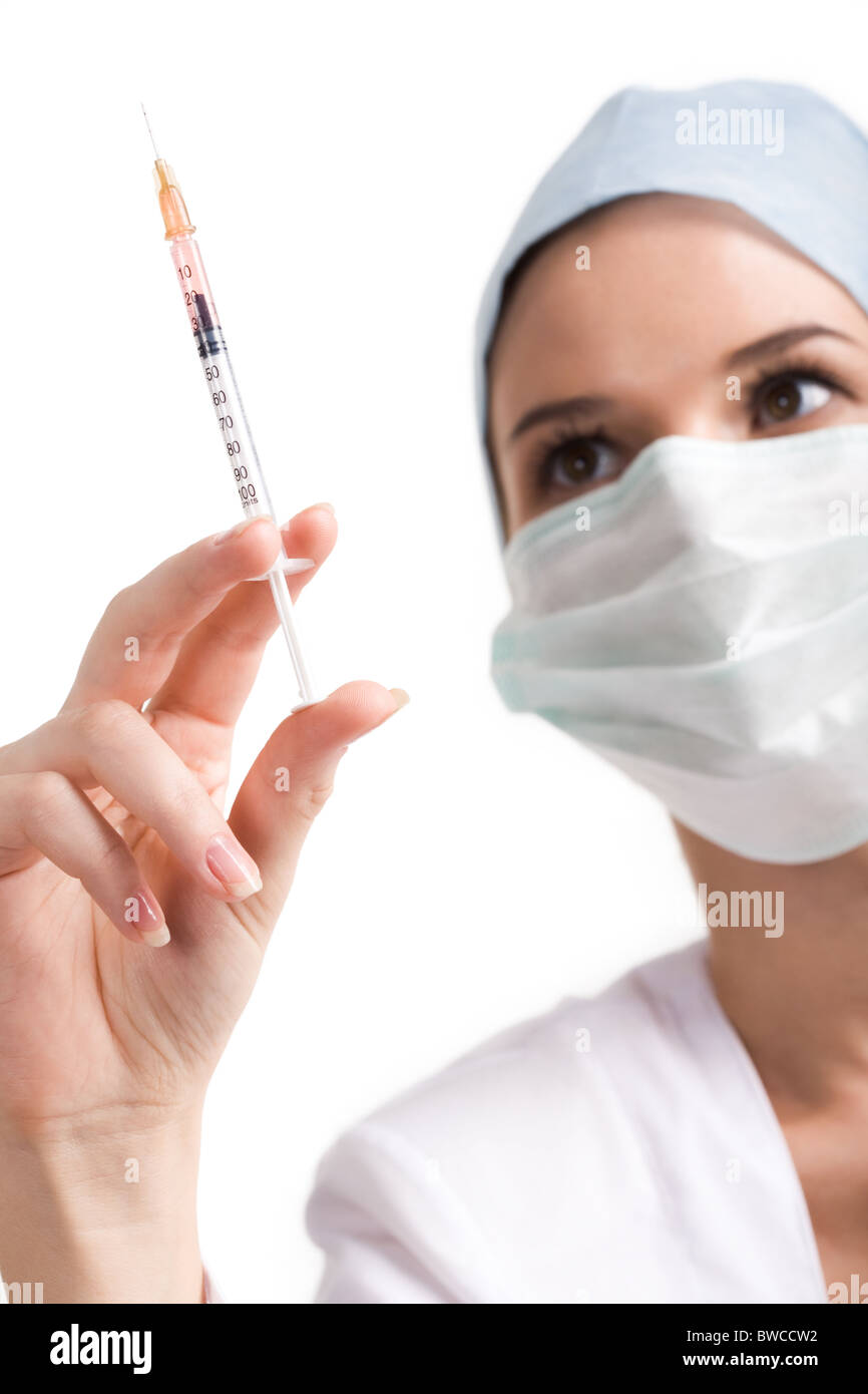 Nurse in mask looking at syringe needle while checking volume of ...