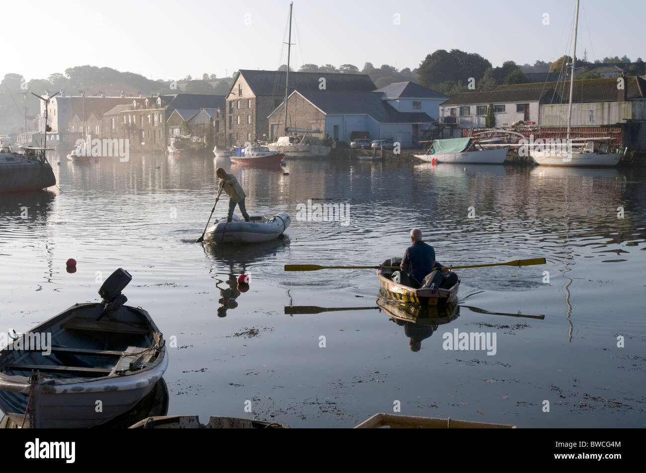 A woman paddles her dinghy on the Penryn river, Cornwall in the early ...