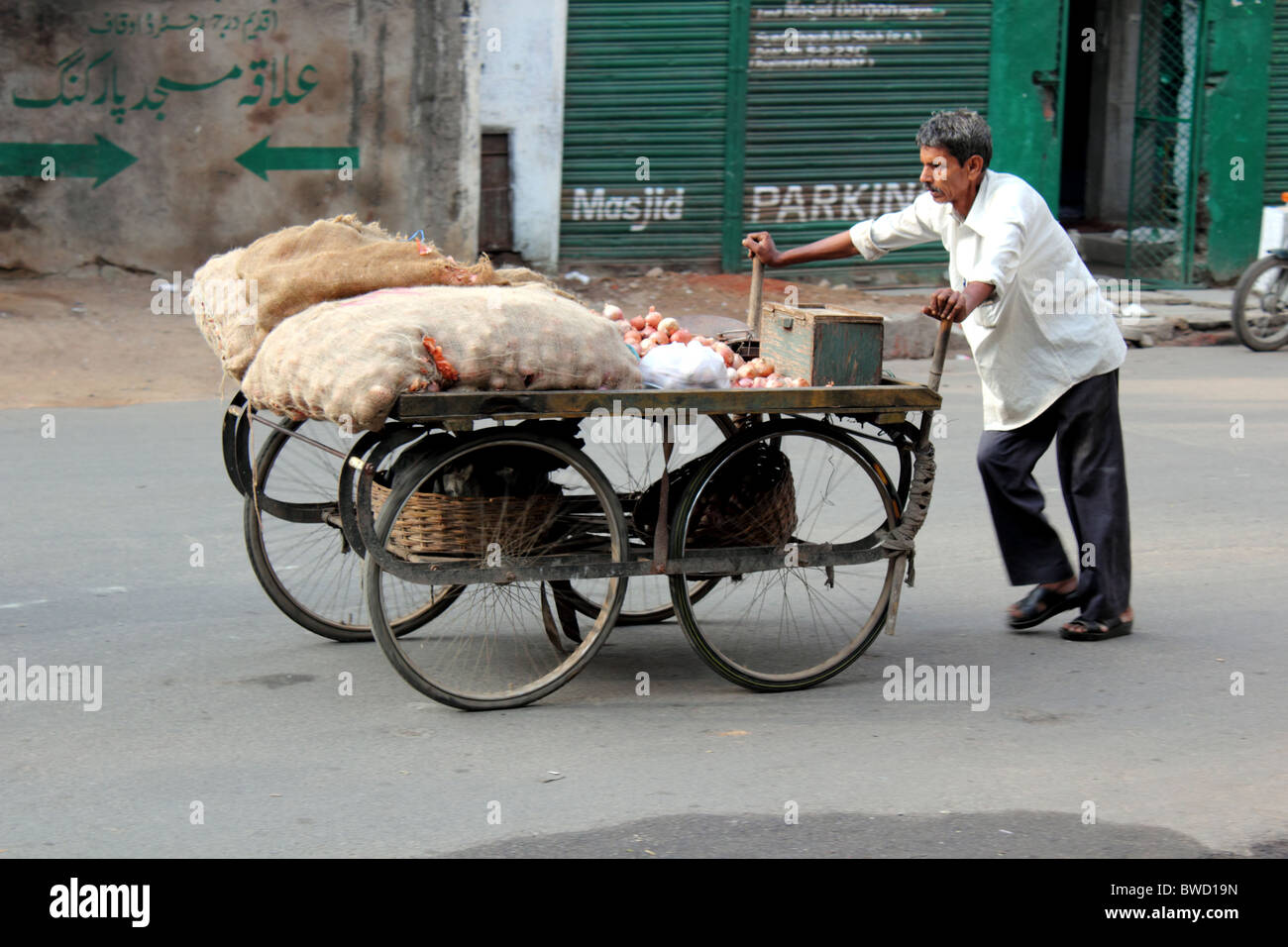 Indian man pushing handcart carrying sacks of fresh vegetables along a ...
