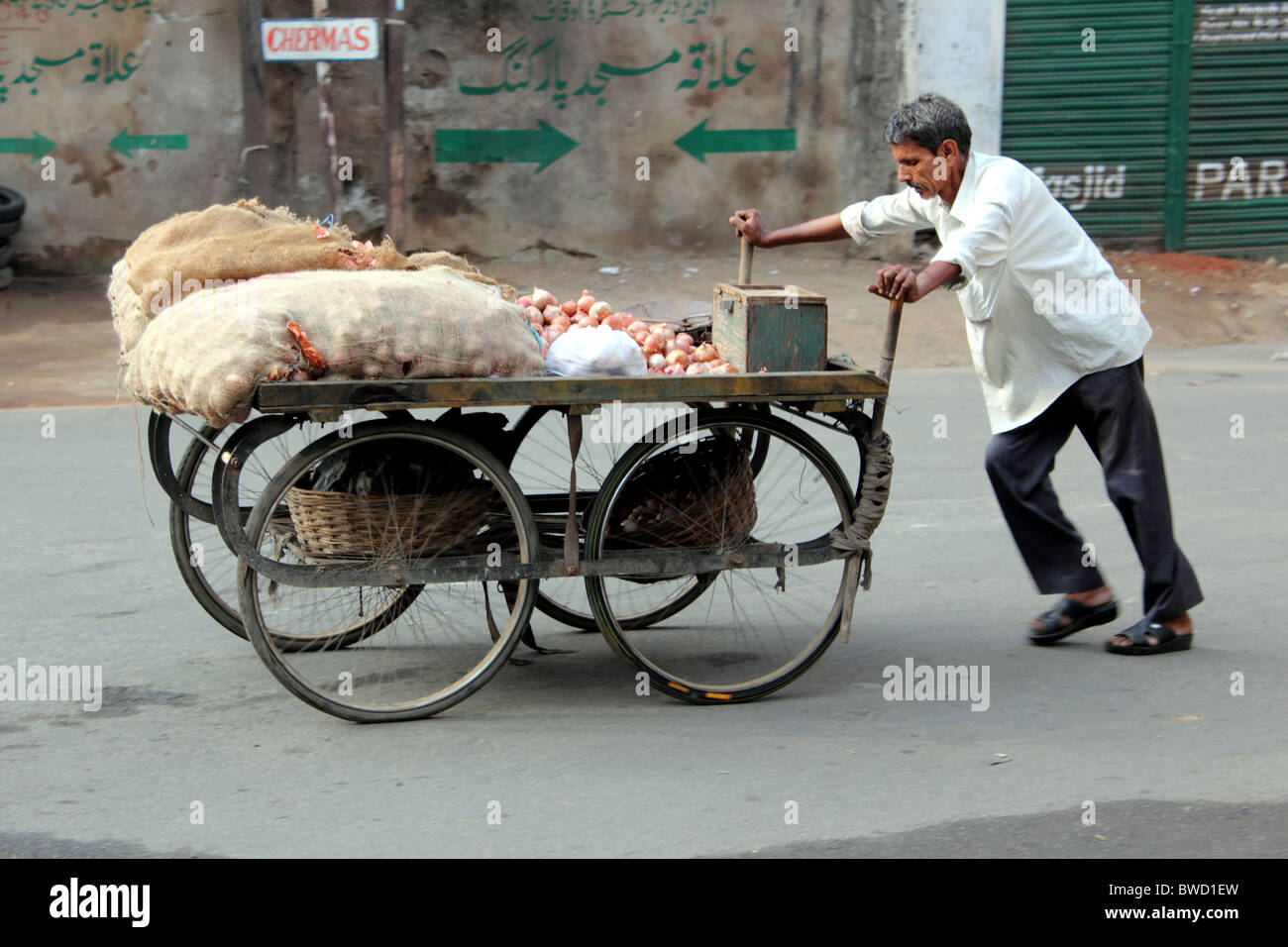 Indian man pushing handcart carrying sacks of fresh vegetables along a ...