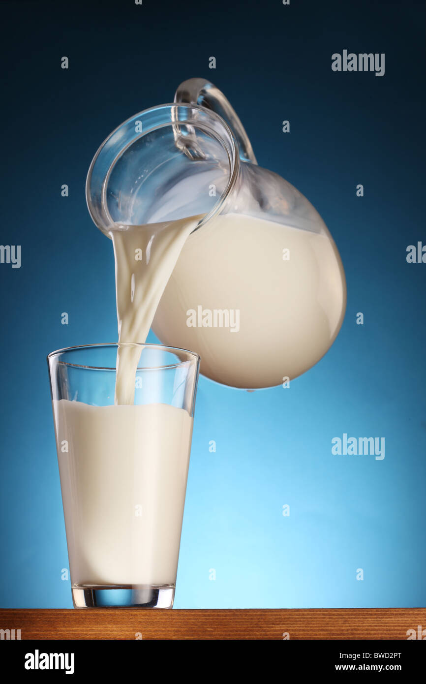 Milk pouring from jar into glass on a blue background Stock Photo - Alamy