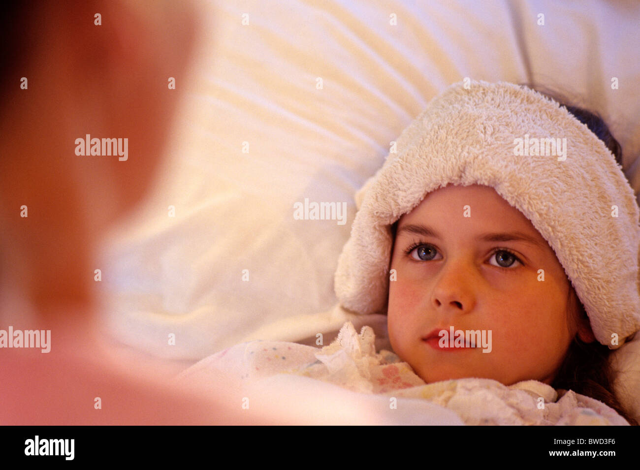 Young girl in bed with flu/cold with mother and wash cloth on forehead ...
