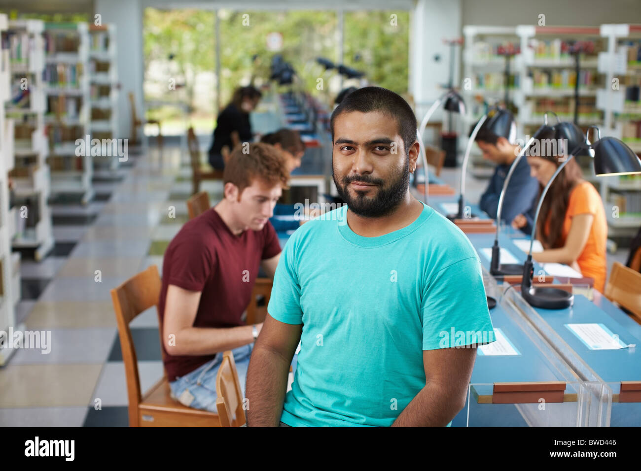 portrait of male college student sitting on table in library and ...