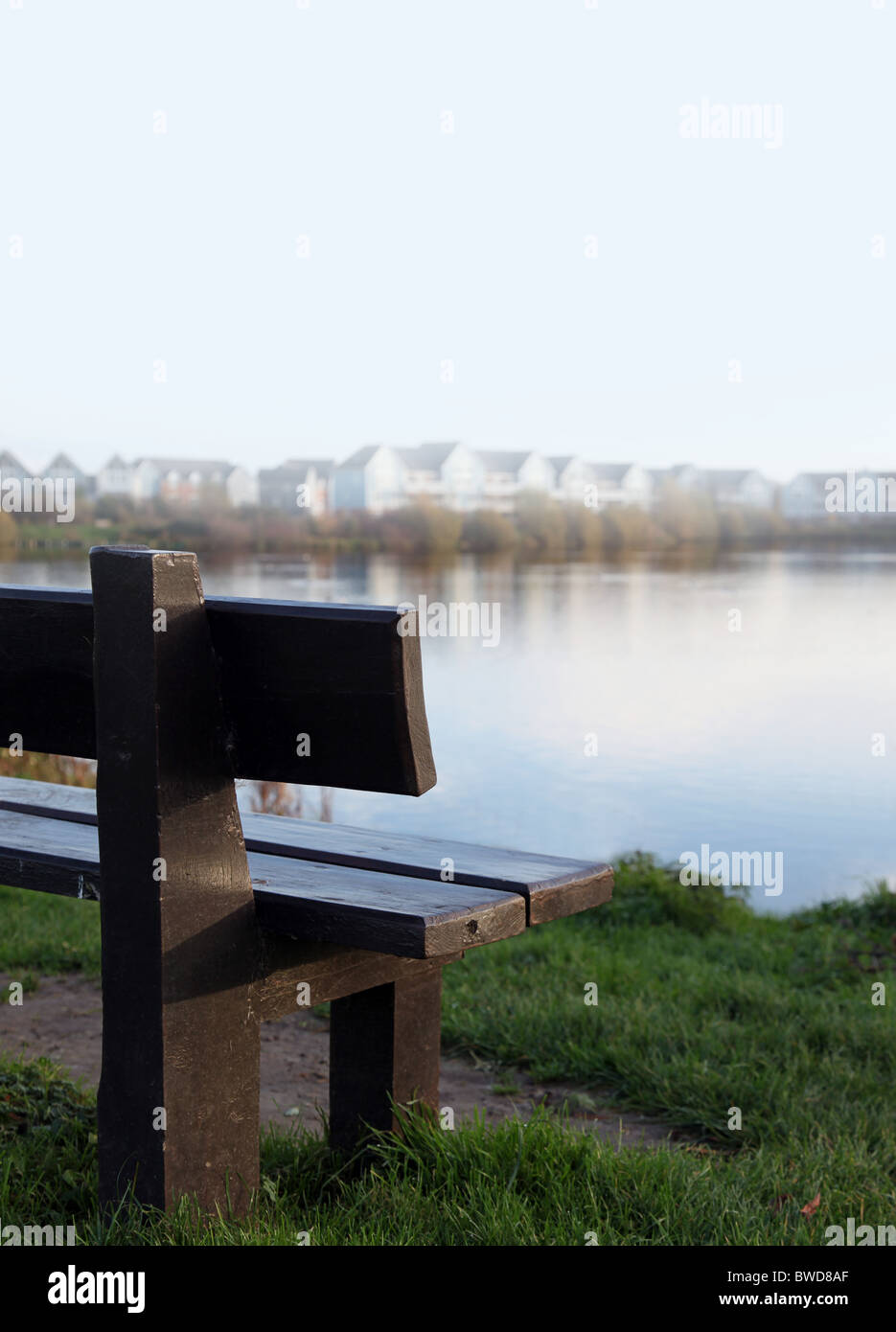 Empty bench overlooking a lake with houses in the distance out of focus ...
