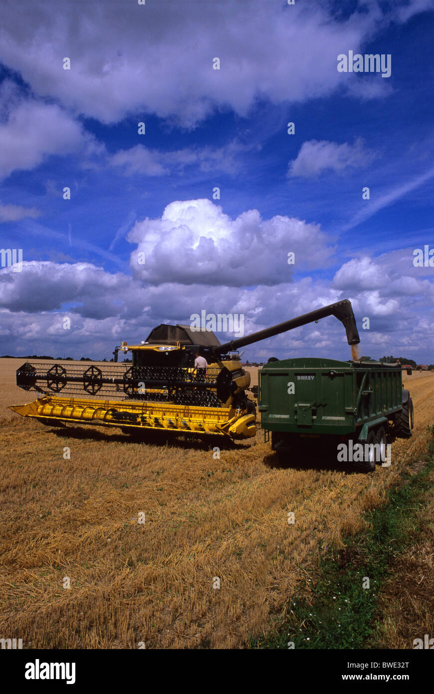 combine harvester emptying harvested grain into trailer at side of ...