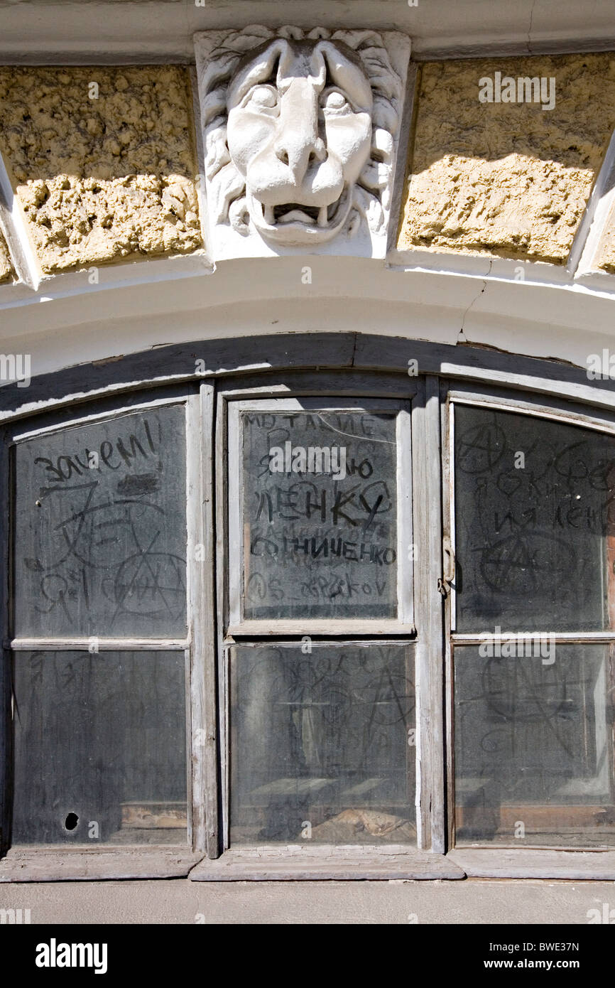 Stucco lion gargoyle over dirty window with graffiti in cyrillic script ...