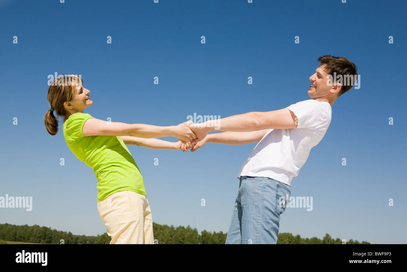 Photo of playful couple holding each other by hands with their arms ...