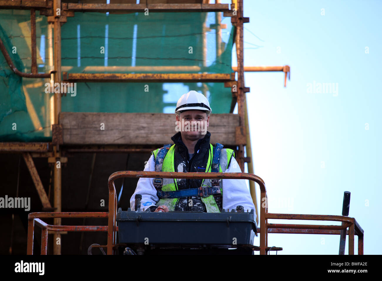 Workman on hoist wearing safety harness and hard hat Stock Photo - Alamy