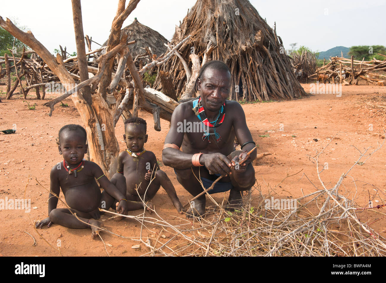 Hamar man with two little children cutting meat in the village, Omo ...