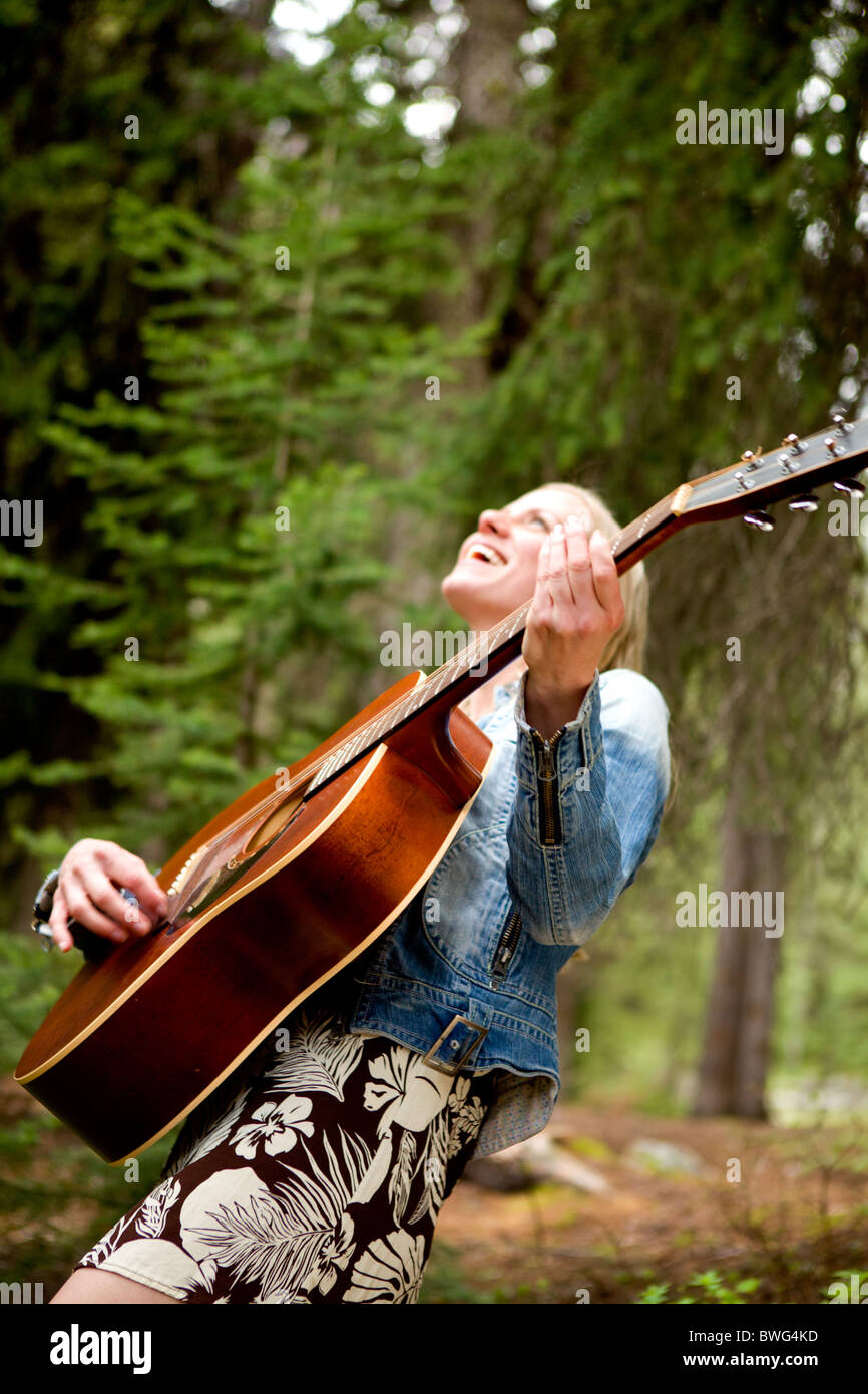 A woman singing freely in the forest with a guitar - sharp focus on ...