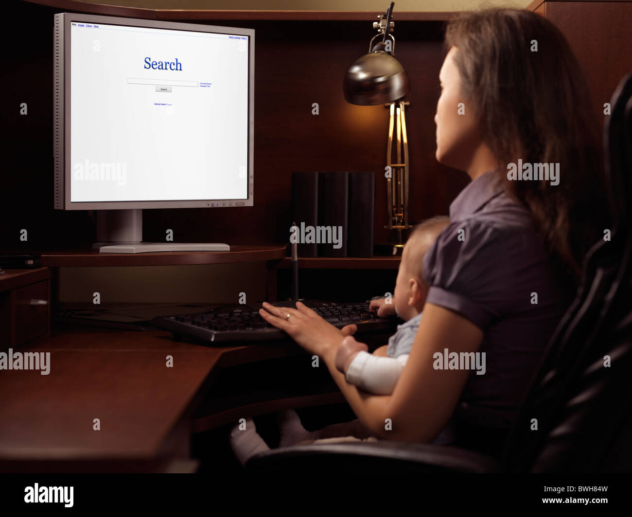 Young woman with a baby sitting at a computer desk with internet search ...