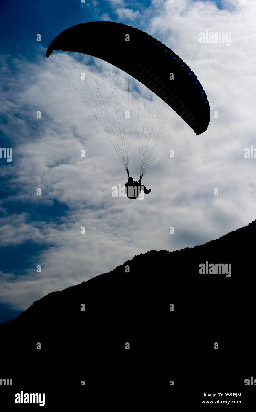 Silhouette of paraglider pilot against dark blue sky with white clouds ...