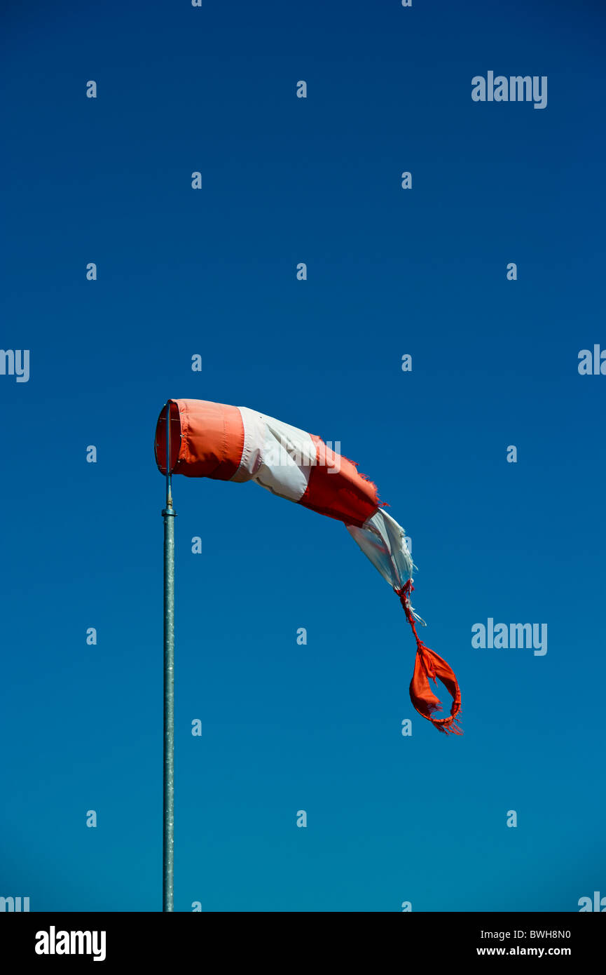 Tattered red and white windsock in light breeze against plain blue sky ...