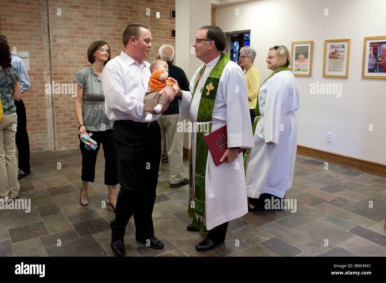 Anglo male pastor greets male church member holding baby after Sunday ...
