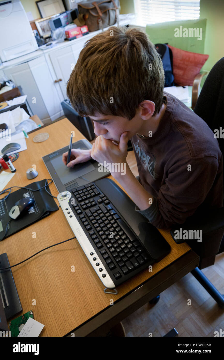 A teenage boy concentrates as he uses a graphics tablet connected to ...