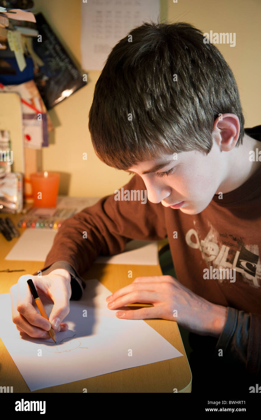 A teenage boy concentrates as he draws a cartoon with pencil and paper ...