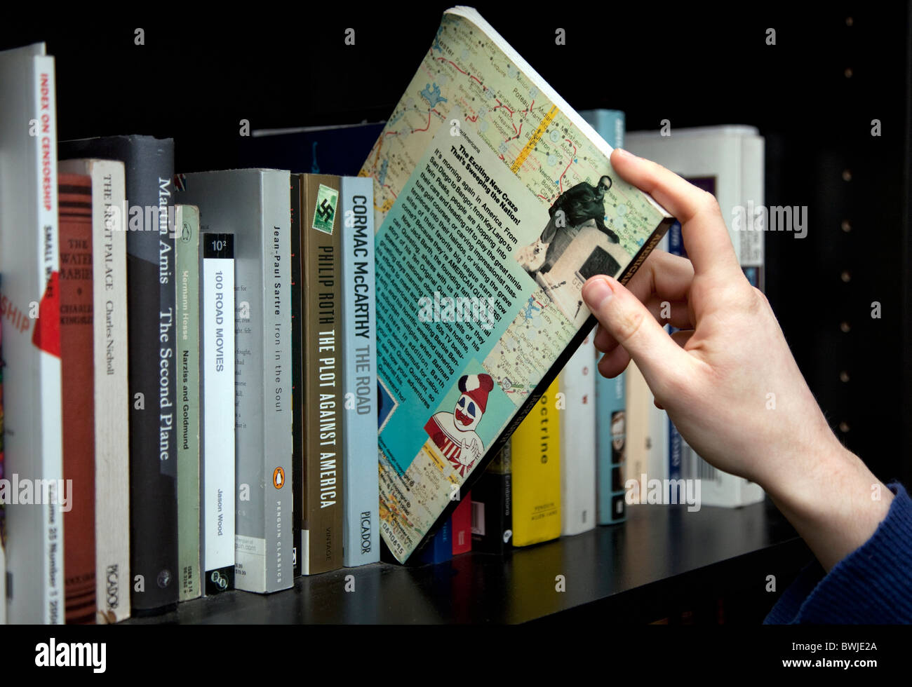 Choosing a book from a bookcase in the home, London Stock Photo - Alamy