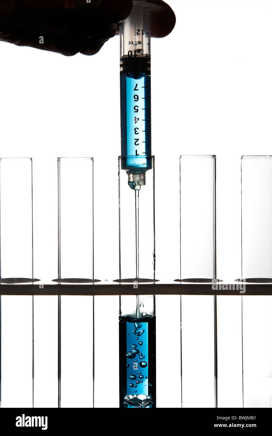 Row of test tubes filled with colored fluid, syringe filling one test ...