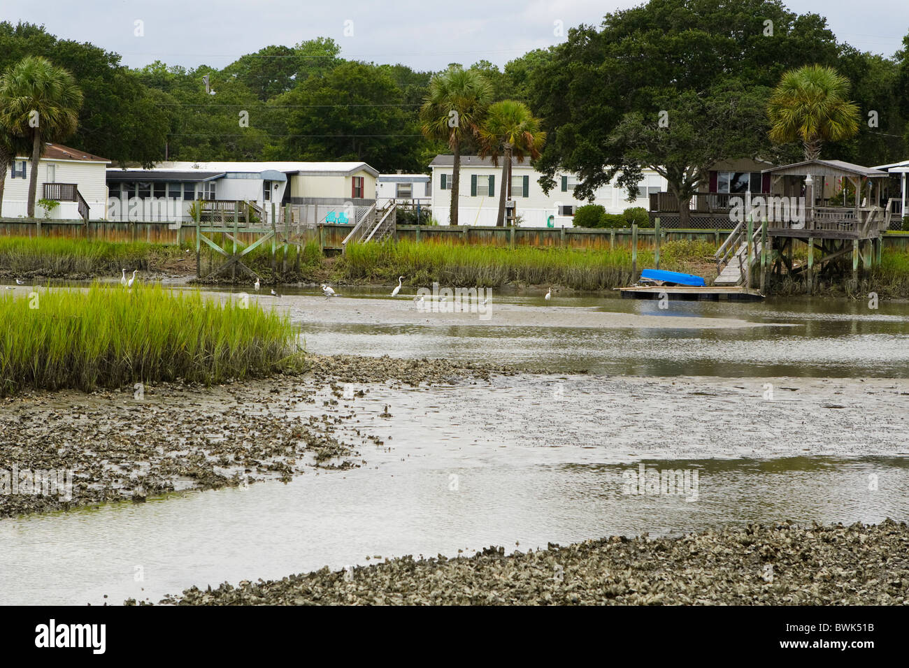 A coastal trailer park & dock sits beside a muddy marsh wetlands stream ...