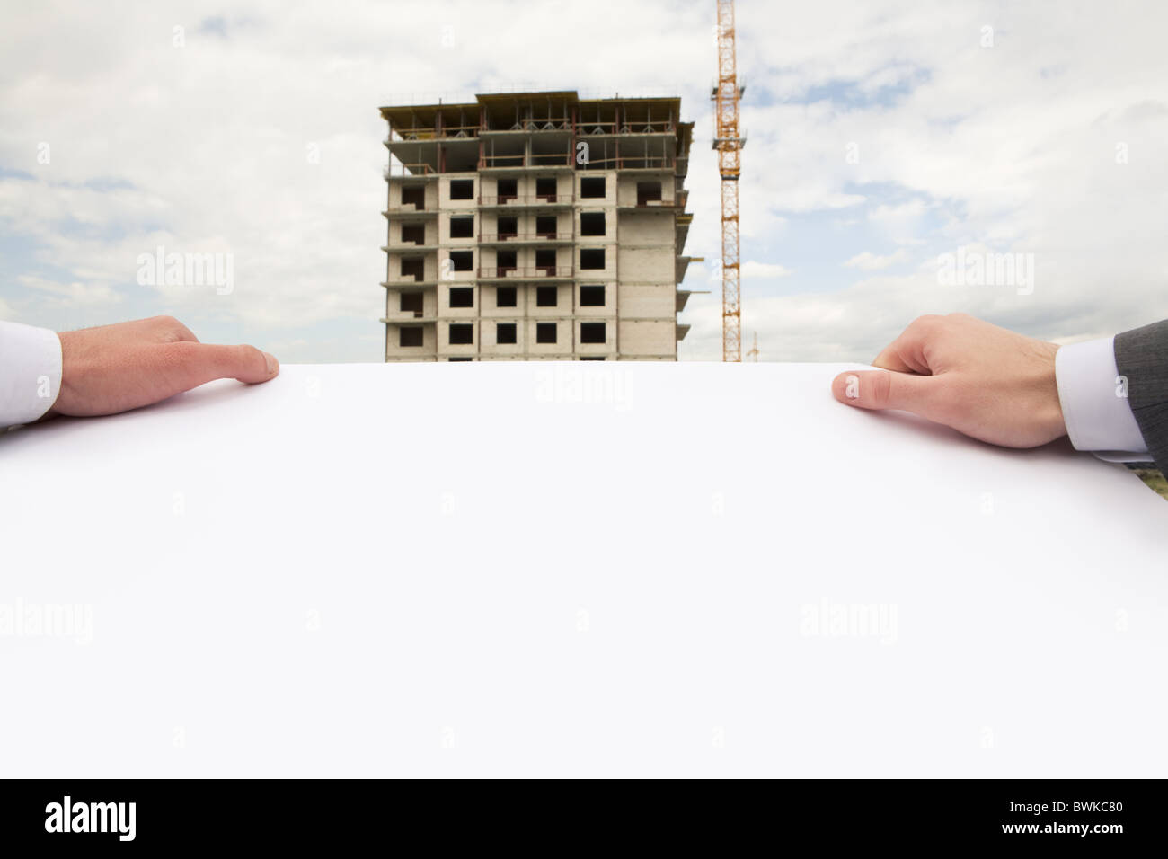 Close-up of builder hands holding blueprint with construction at ...
