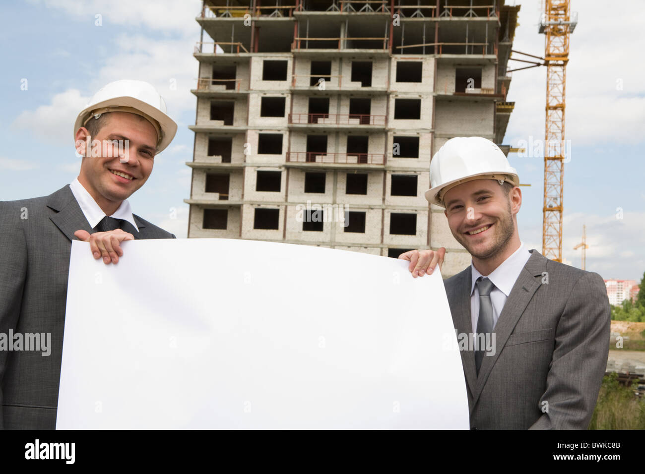 Portrait of two successful builders holding large sheet of paper with ...