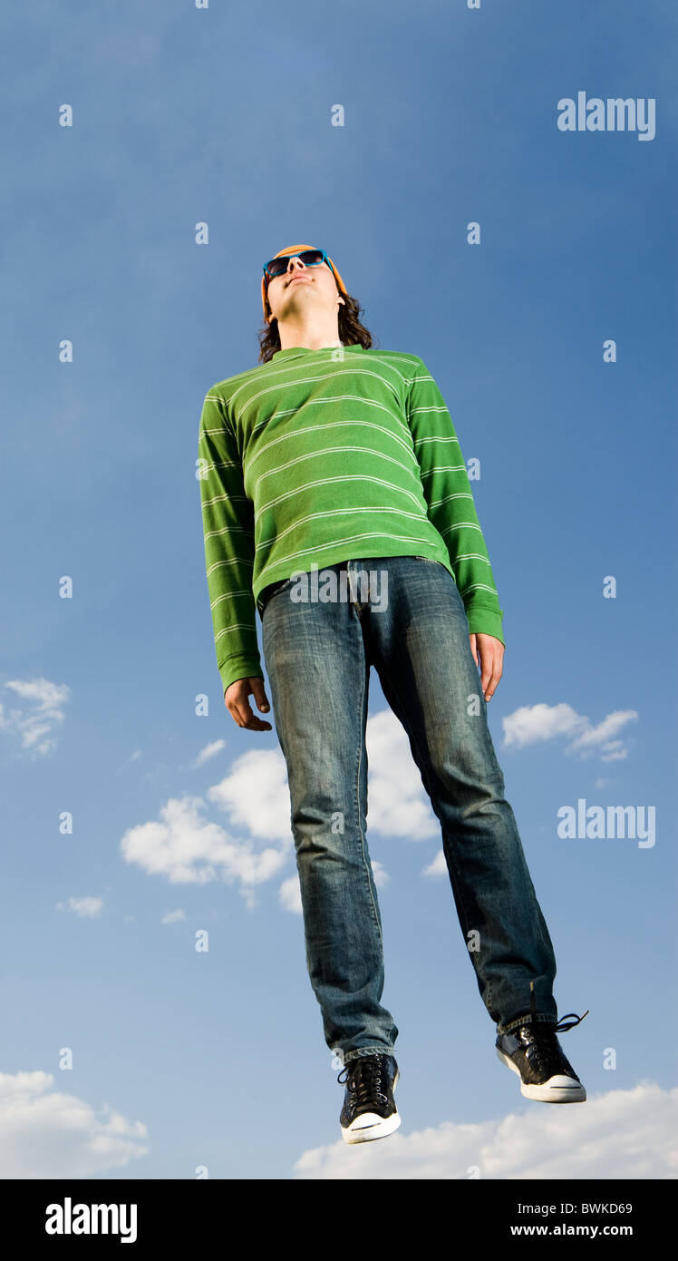 Portrait of casually dressed man in high jump against bright blue sky ...