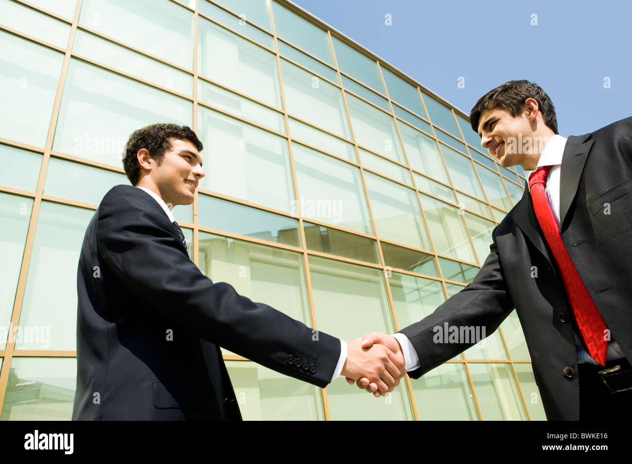 Photo of successful men handshaking at background of modern building ...