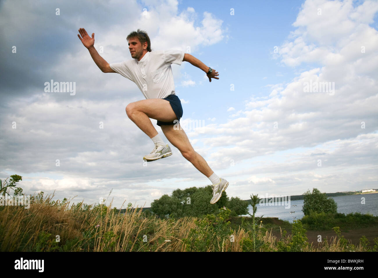 Horizontal image of active man jumping near lake Stock Photo - Alamy