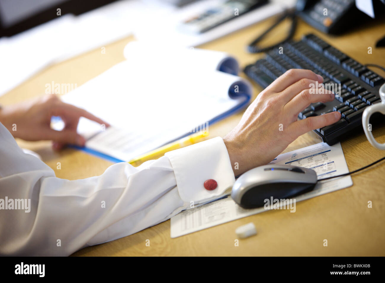 Person in an office typing data from a sheet of paper into a computer ...
