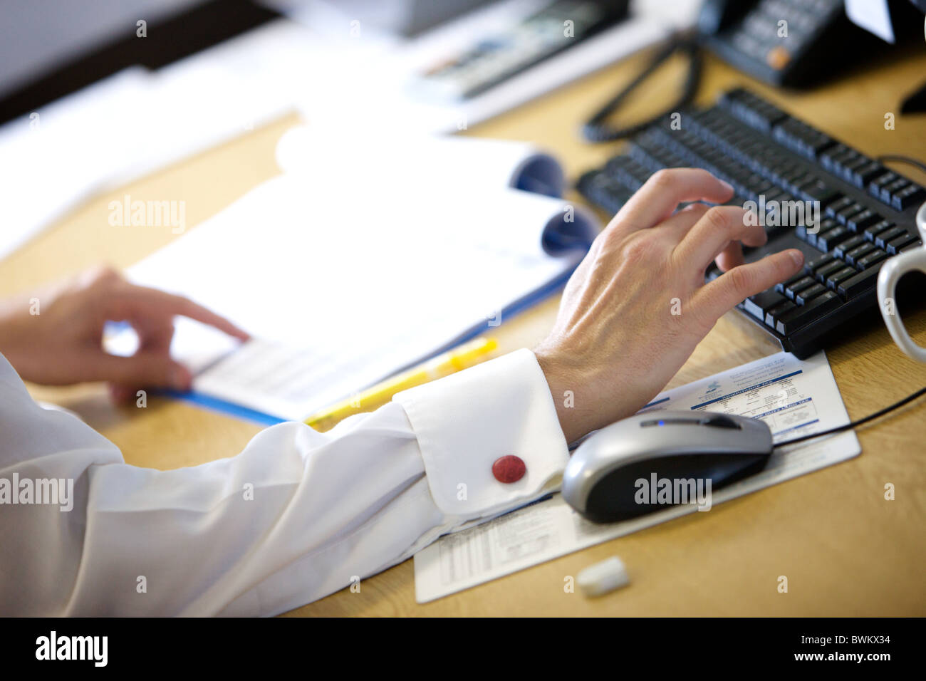 Person in an office typing data from a sheet of paper into a computer ...