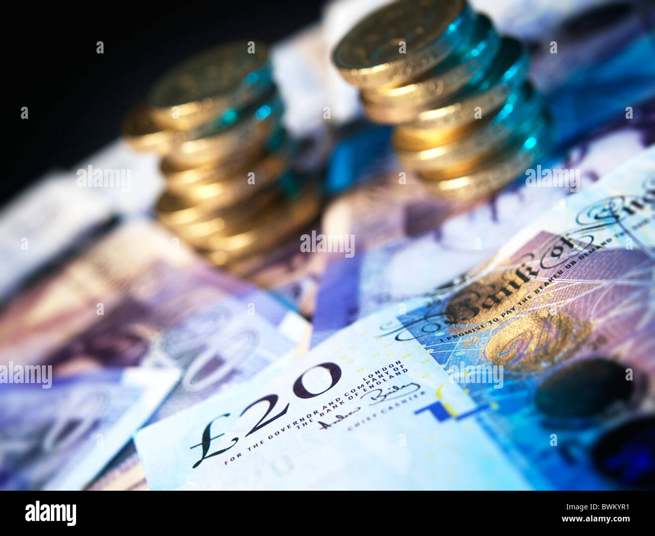 British pound coins stacked in background on a bed of twenty pound ...