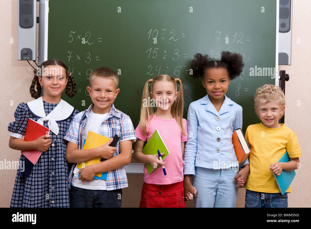 Image of curious schoolchildren standing by blackboard and looking at ...