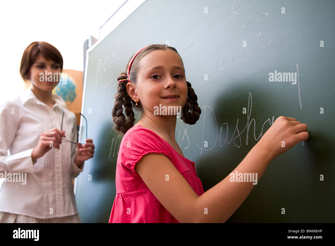 Photo of smart schoolgirl writing on blackboard with teacher at ...