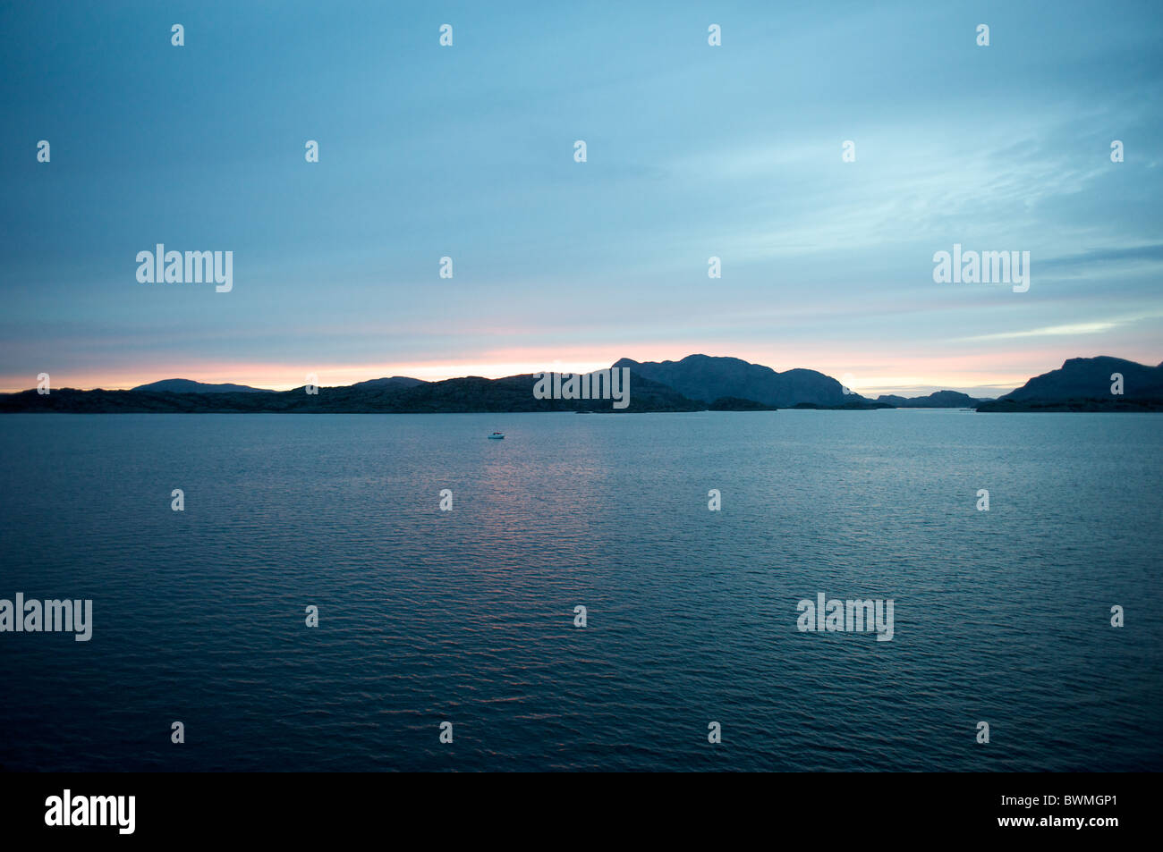 A small motor boat in the distance with people on board as sun sets in ...